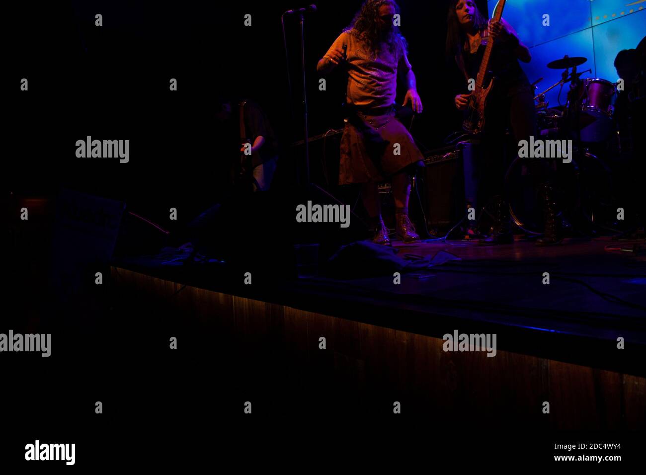 Male vocalist dancing wearing kilt while guitarist, bassist and drummer ...