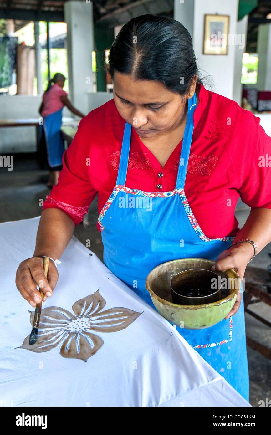 A worker applies wax to a batik using a canting tool prior to the ...