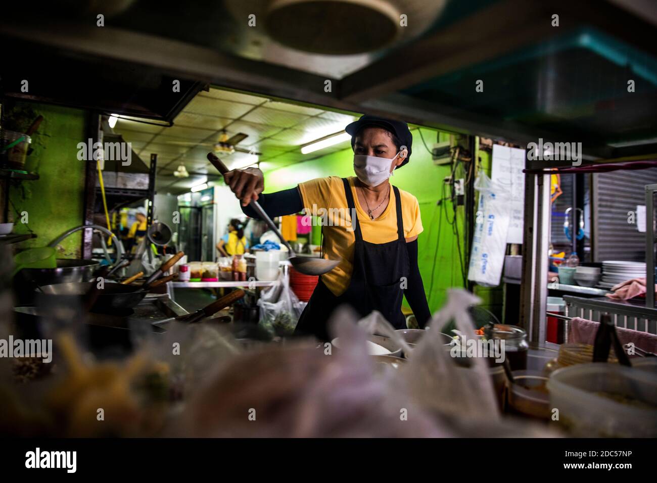 A masked cook works on a food order for a customer of her restaurant on ...