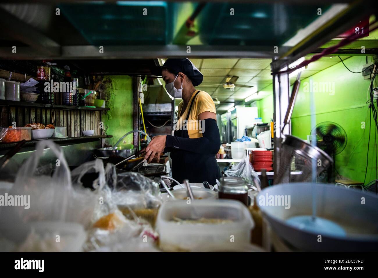 A masked cook works on a food order for a customer of her restaurant on ...