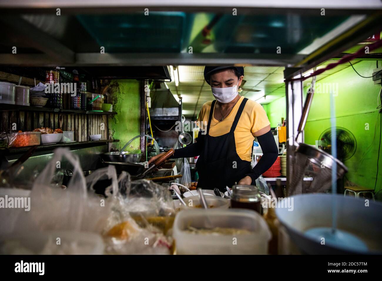 A masked cook works on a food order for a customer of her restaurant on ...