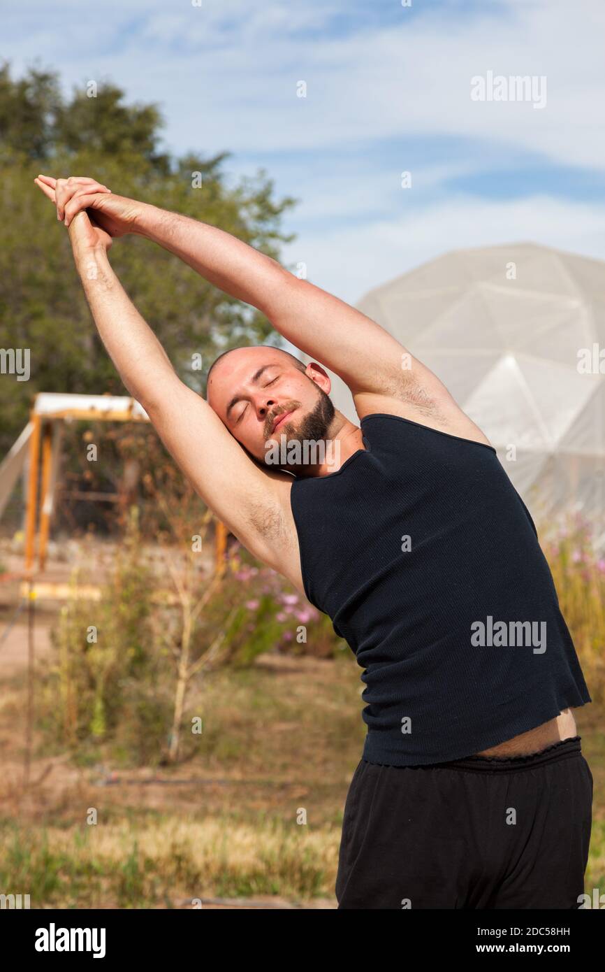 A man bends to the side with his arms over his head as he participates ...