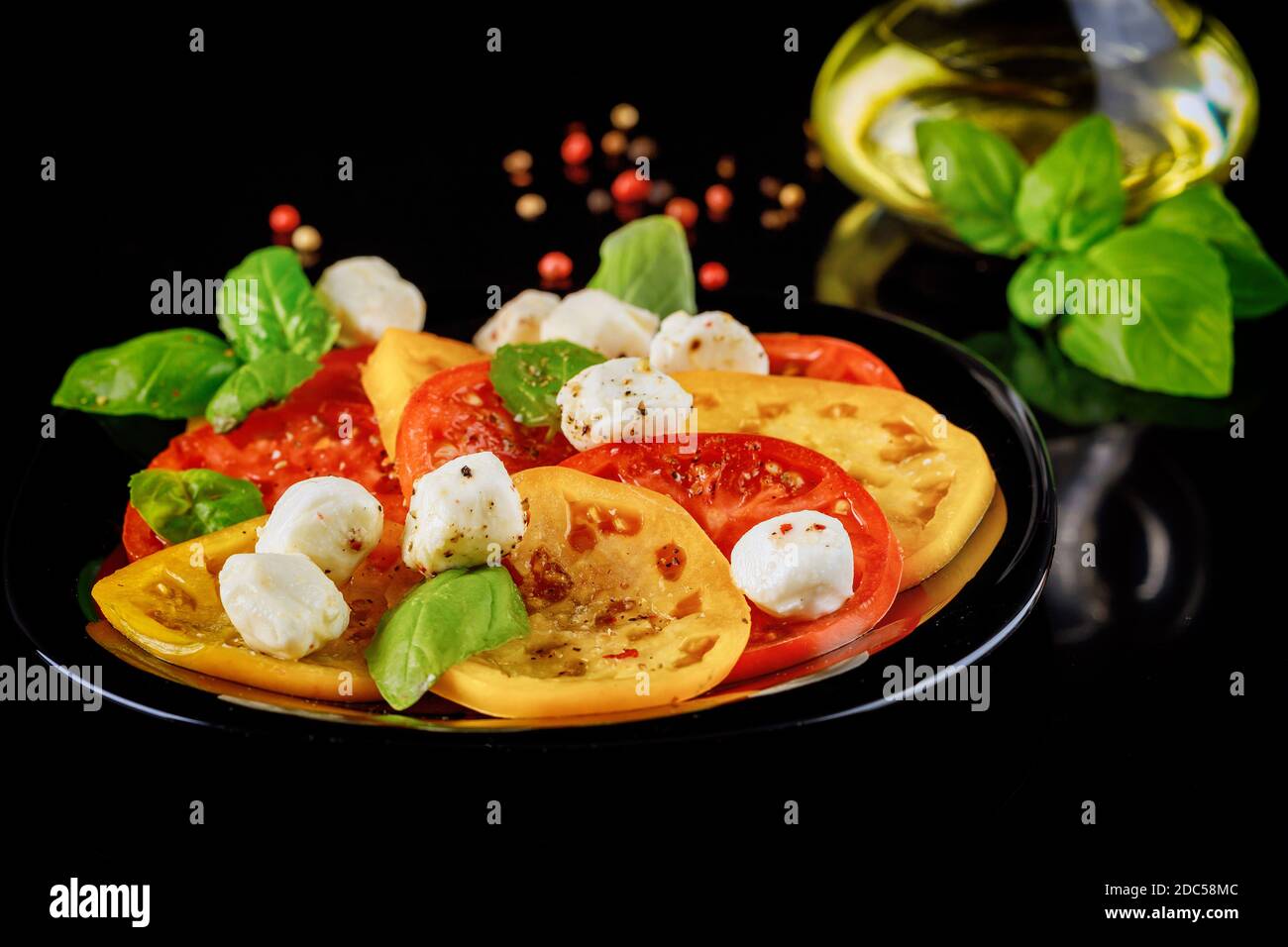 Sliced tomato with mozzarella, basil and olive oil on black background ...