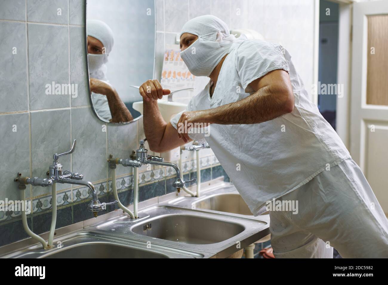 A surgeon turns off the water tap with his elbow after washing his ...