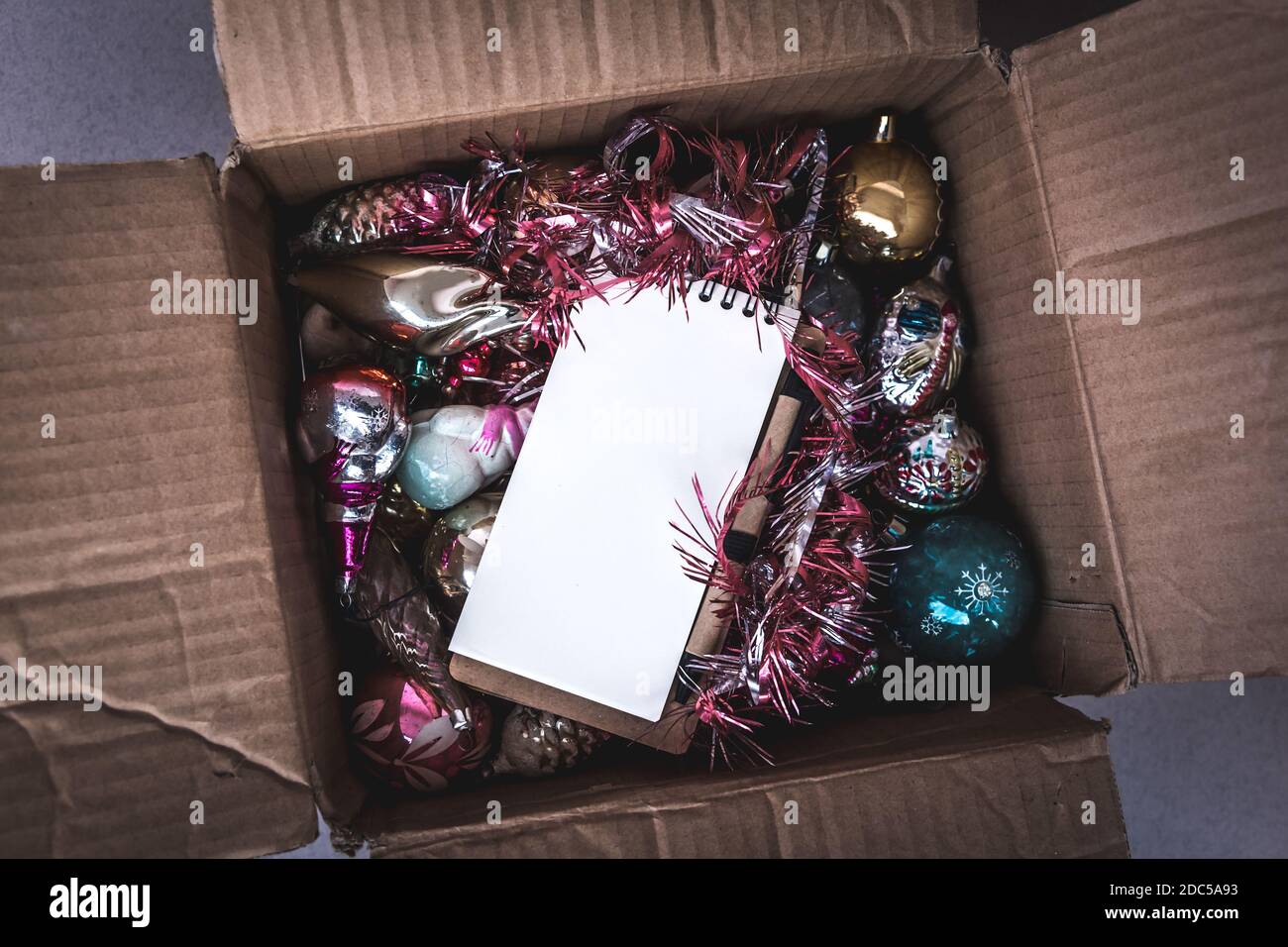 An open cardboard box with old glass Christmas decorations. On top of a ...
