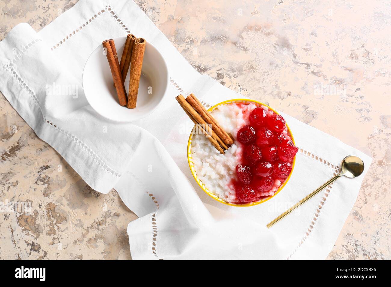 Bowl of tasty rice pudding with cherry and cinnamon on white napkin ...