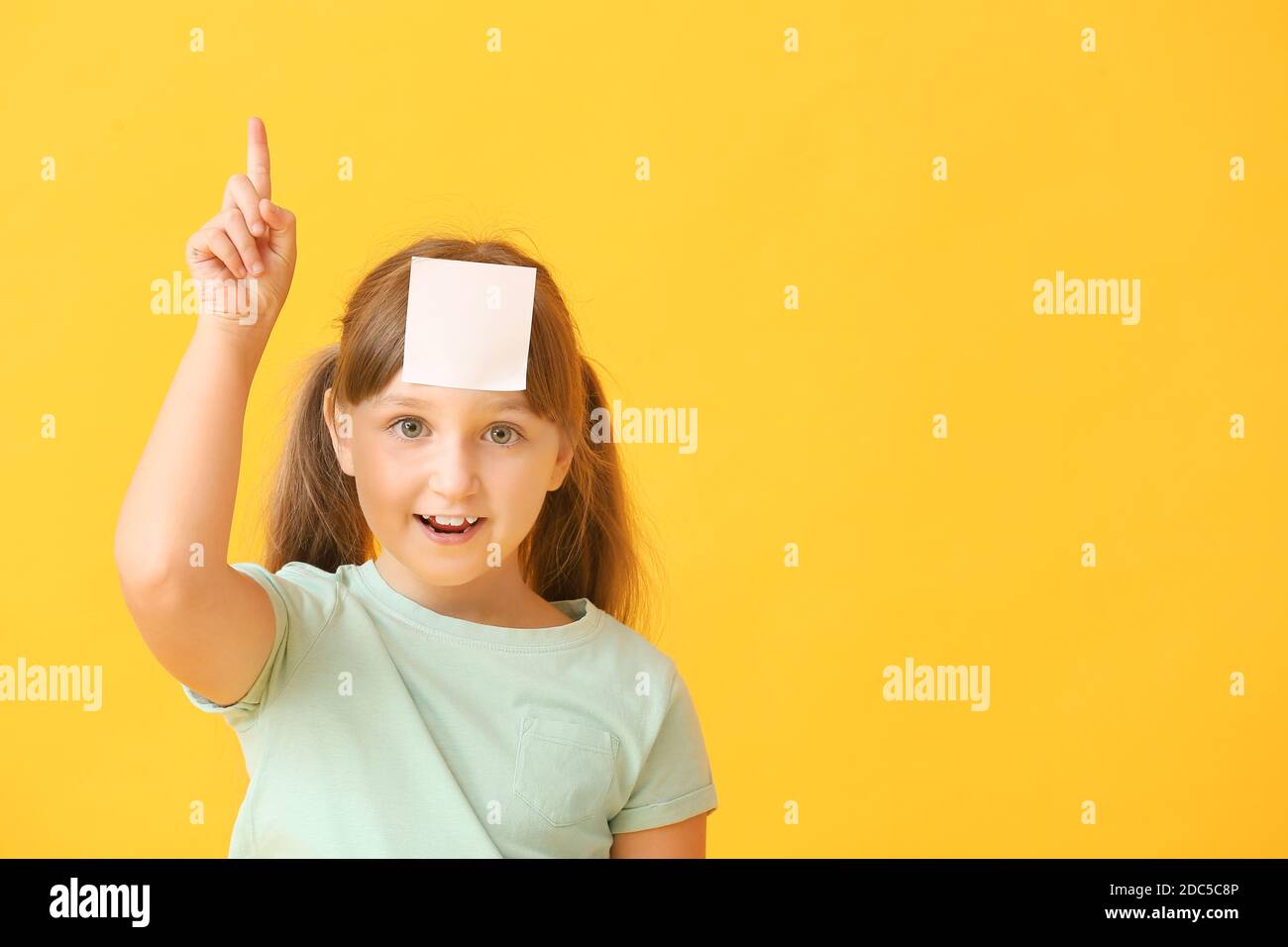 Little girl with blank note paper on her forehead against color ...