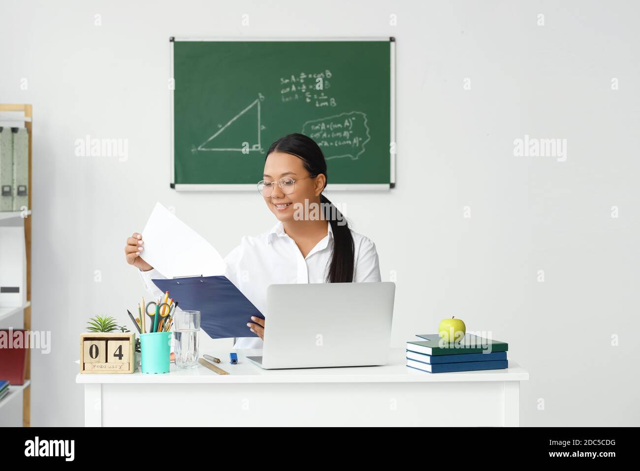 Asian female teacher sitting at table in classroom Stock Photo - Alamy