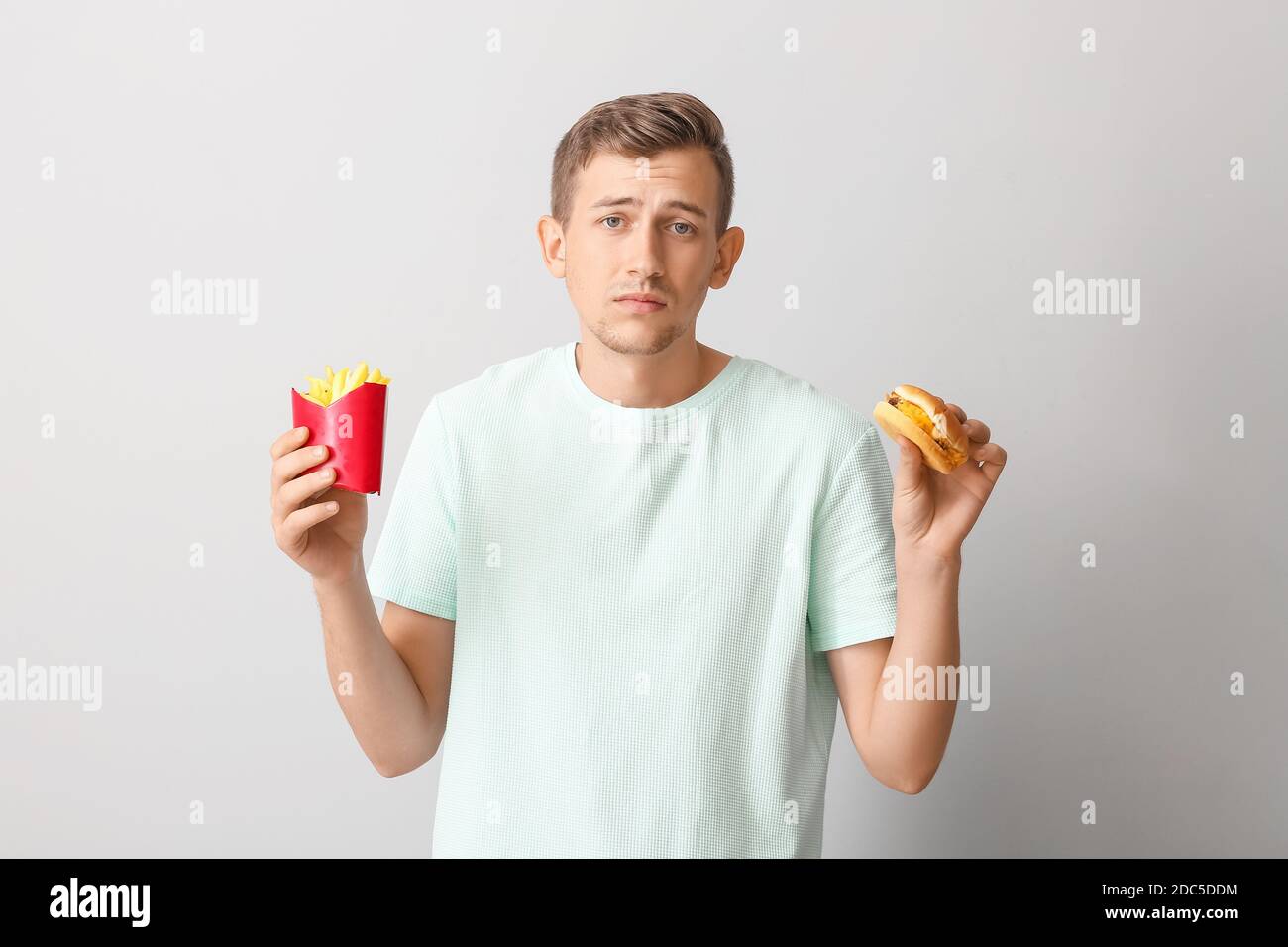 Sad young man with french fries and burger on light background Stock ...