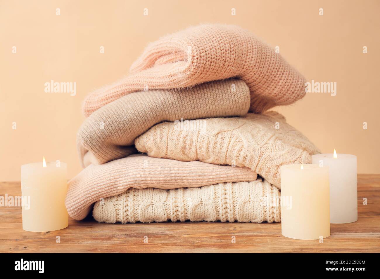 Stylish warm clothes with candles on table against color background ...