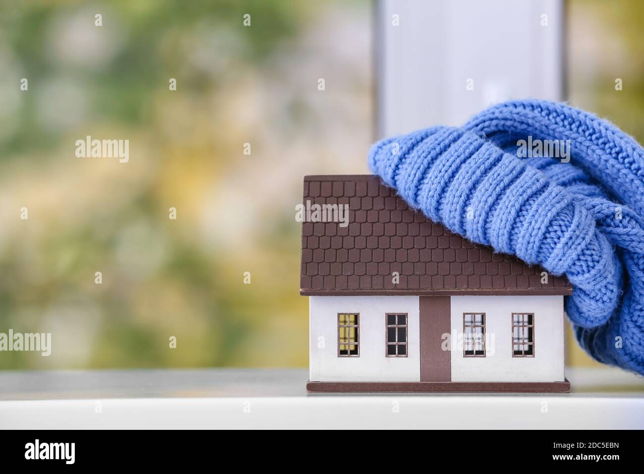 Figure of house and warm hat on window sill. Concept of heating season ...