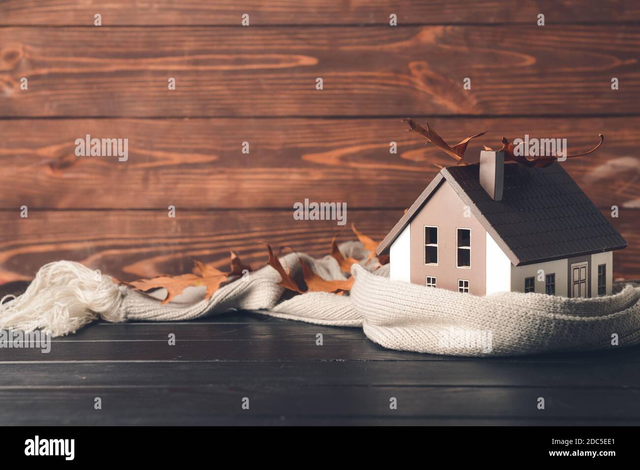 Figure of house, autumn leaves and warm scarf on table. Concept of ...