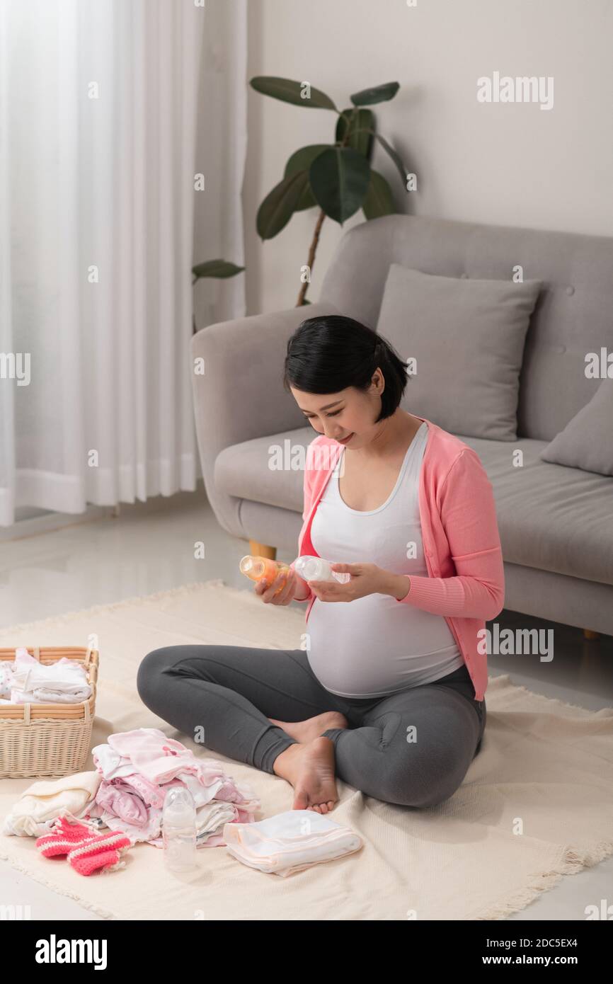 a pregnant woman at home on the floor checking list of baby clothes ...