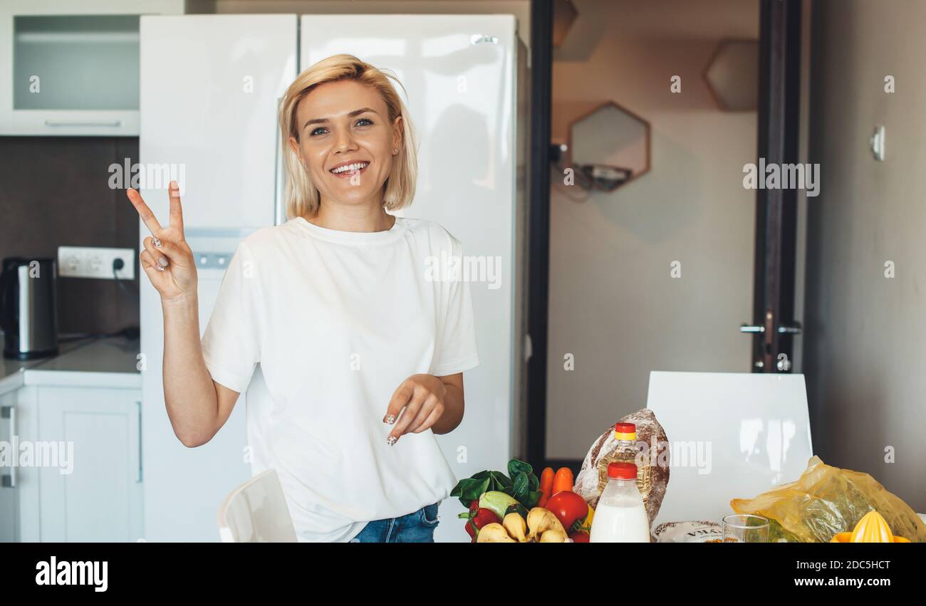 Blonde woman is gesturing the peace sign while unpacking food in the ...