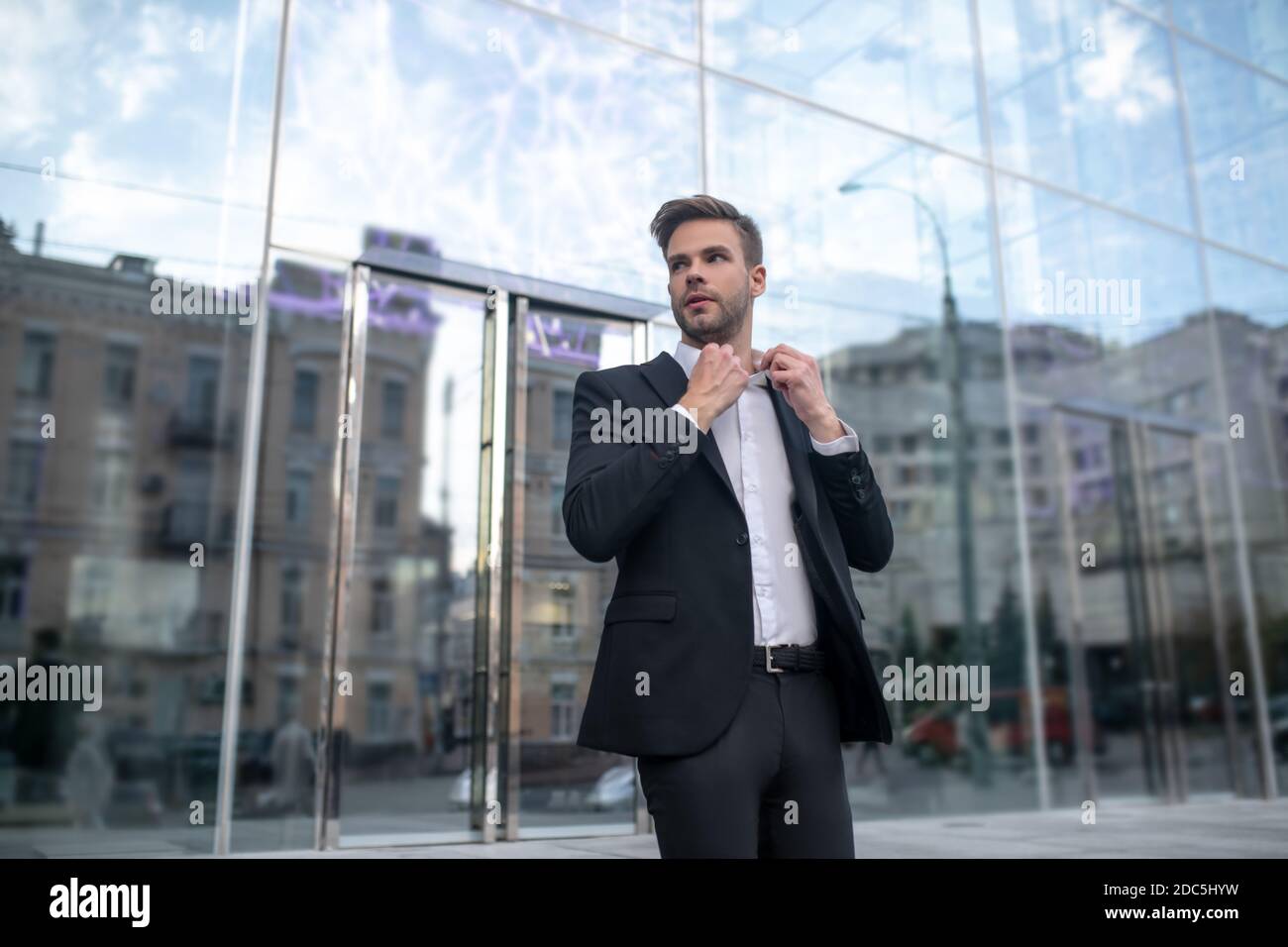 Elegant young man in a black suit fixing his collar Stock Photo - Alamy