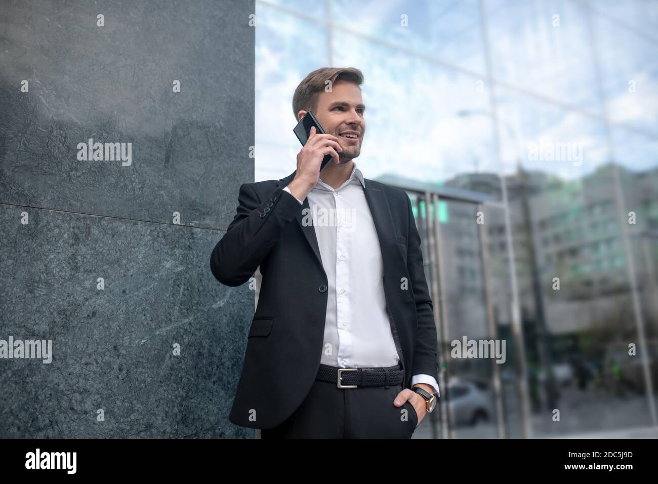 Elegant young man in a black suit talking on the phone Stock Photo - Alamy