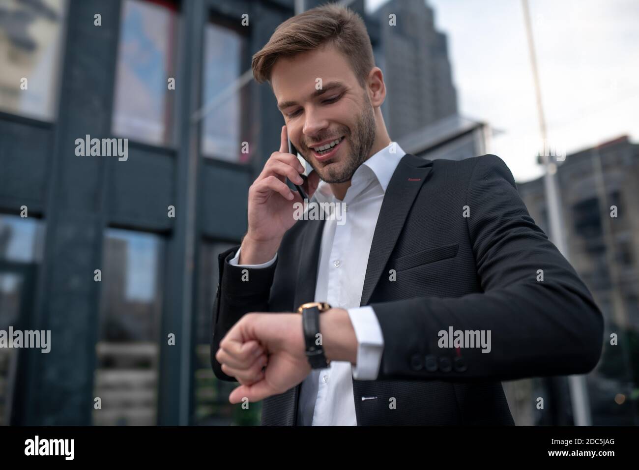 Young man in a black suit talking on the phone and making an ...