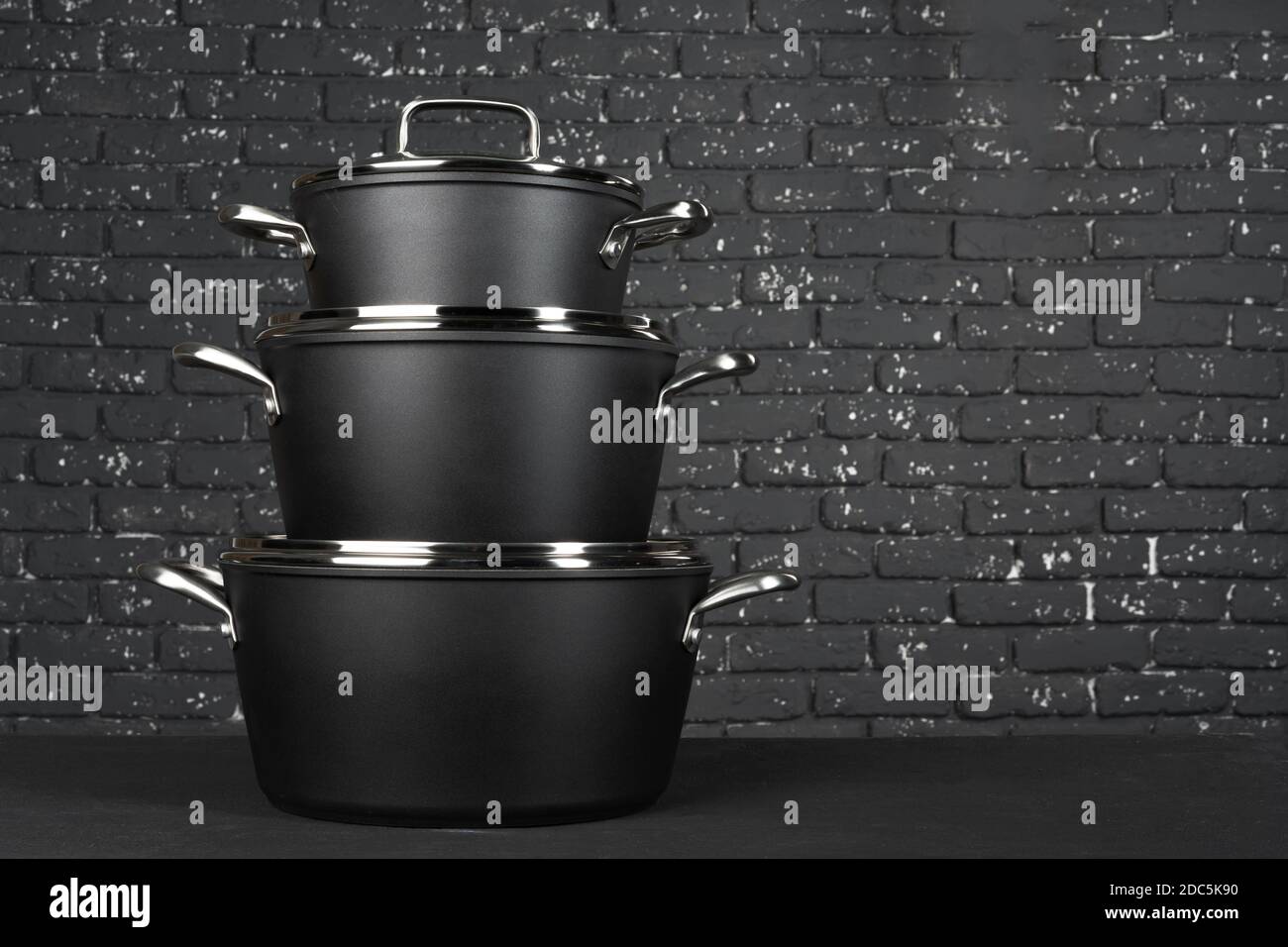 Stack of black cooking pots against black brick background Stock Photo ...