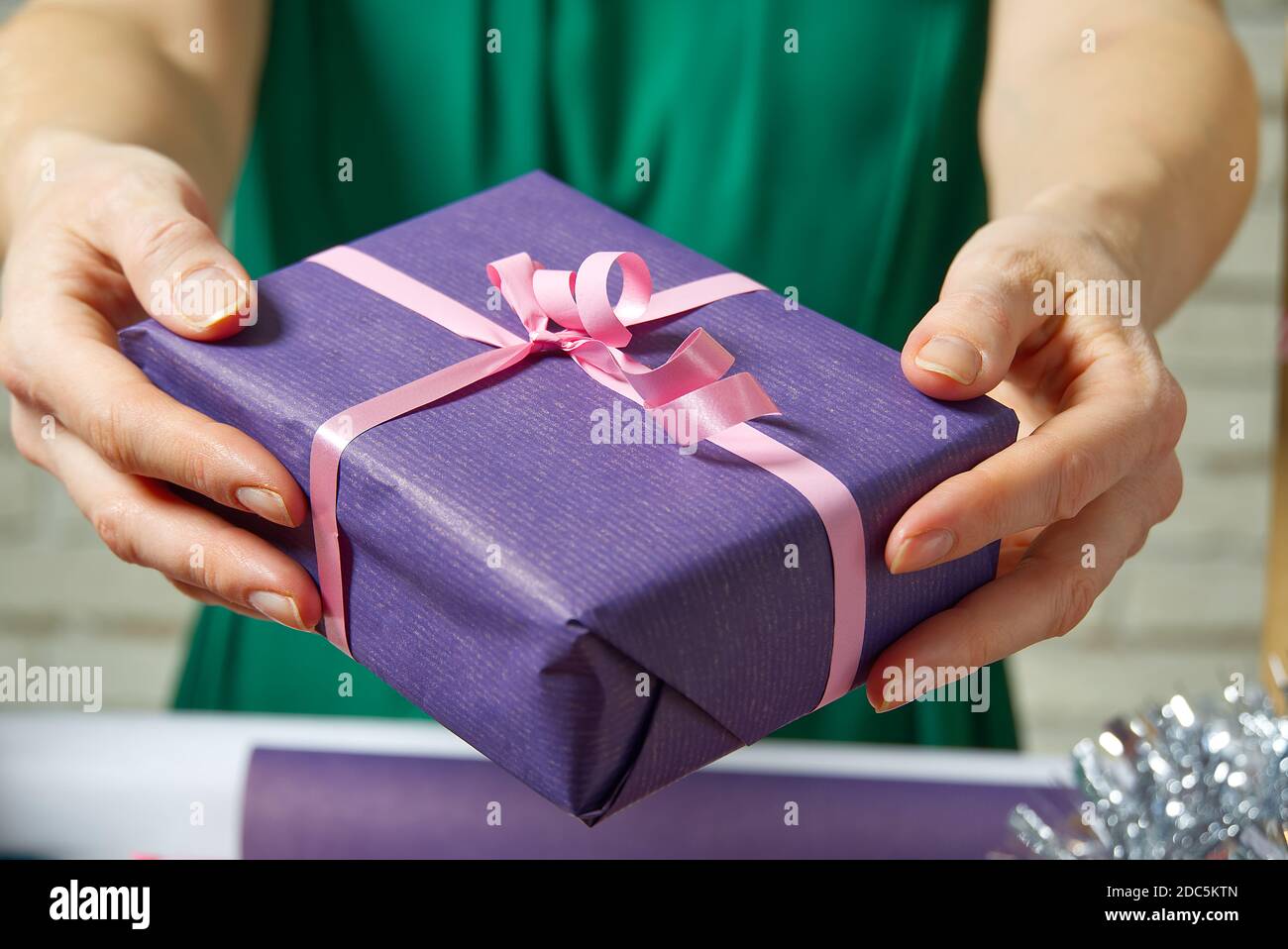 Female hands holding a small gift box wrapped in packing paper. To give ...
