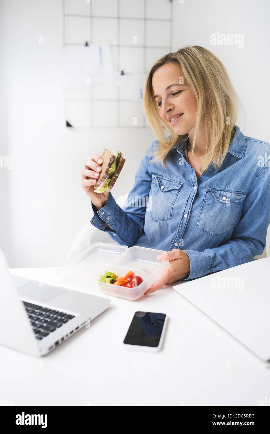 Pretty woman eating whole wheat bread while working in office Stock ...