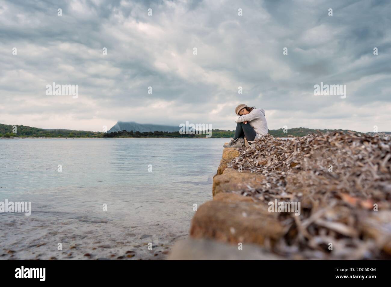 Young woman alone on an old stone jetty on the sea with dramatic sky at ...