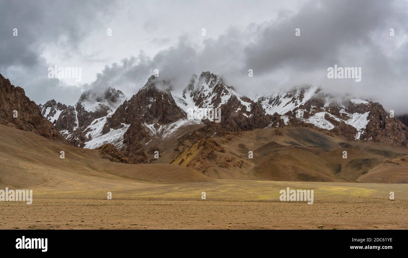 Rain, clouds and orange colored mountains with snow at the Pamir ...