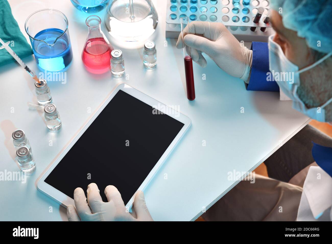 Lab worker using tablet with blood sample on workbench with vials and ...