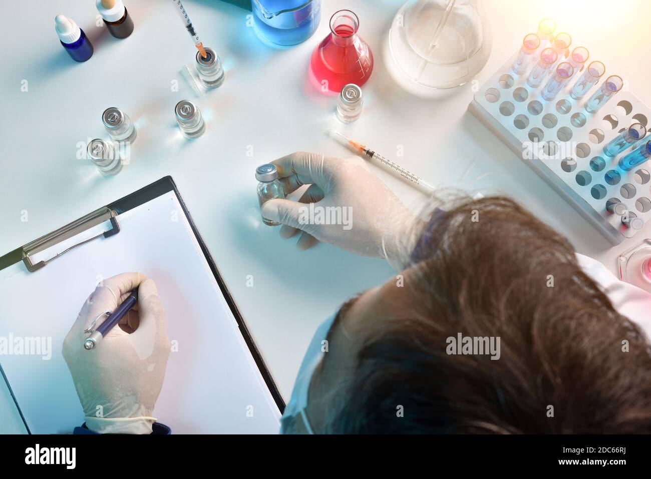 Laboratory technician writing on notepad with vial in hand on a ...