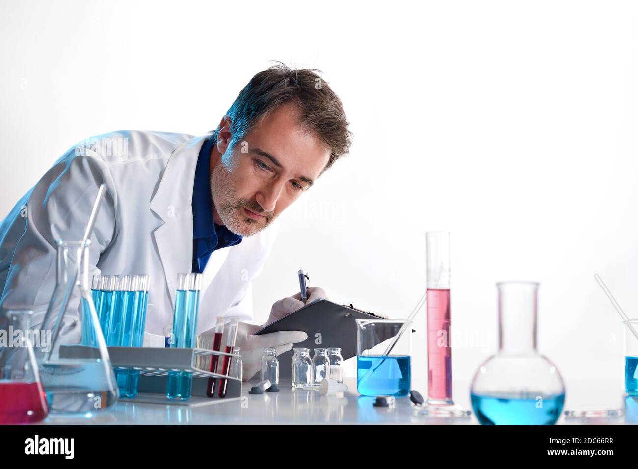 Scientist writing in a notebook on a laboratory table with glassware ...