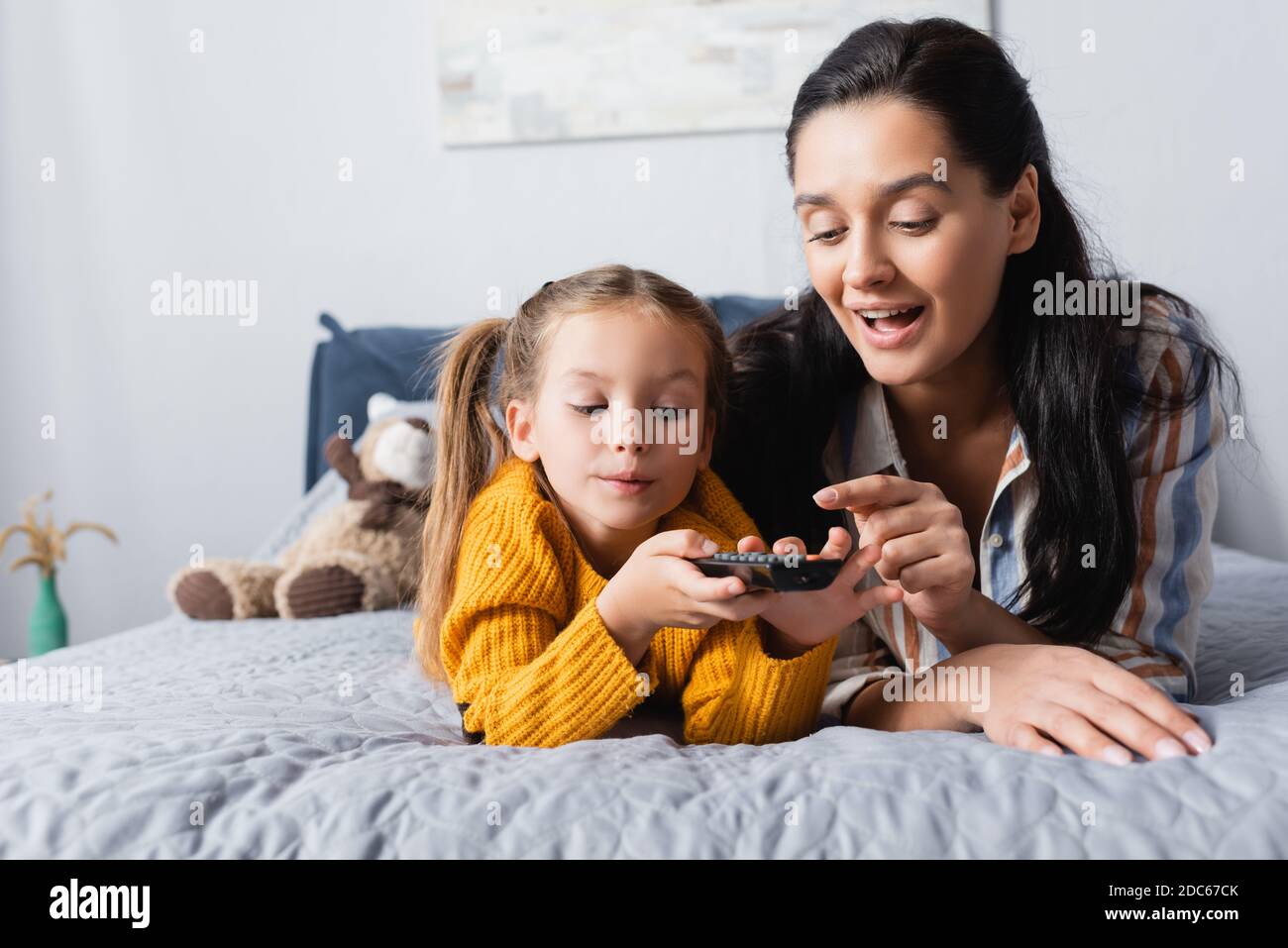 happy mother showing daughter how to use tv remote controller while ...