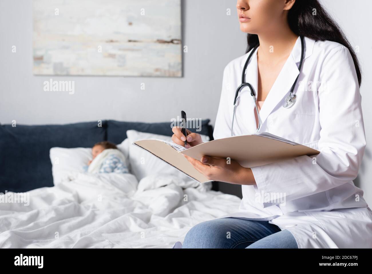 pediatrician writing in outpatient card near ill girl lying in bed ...