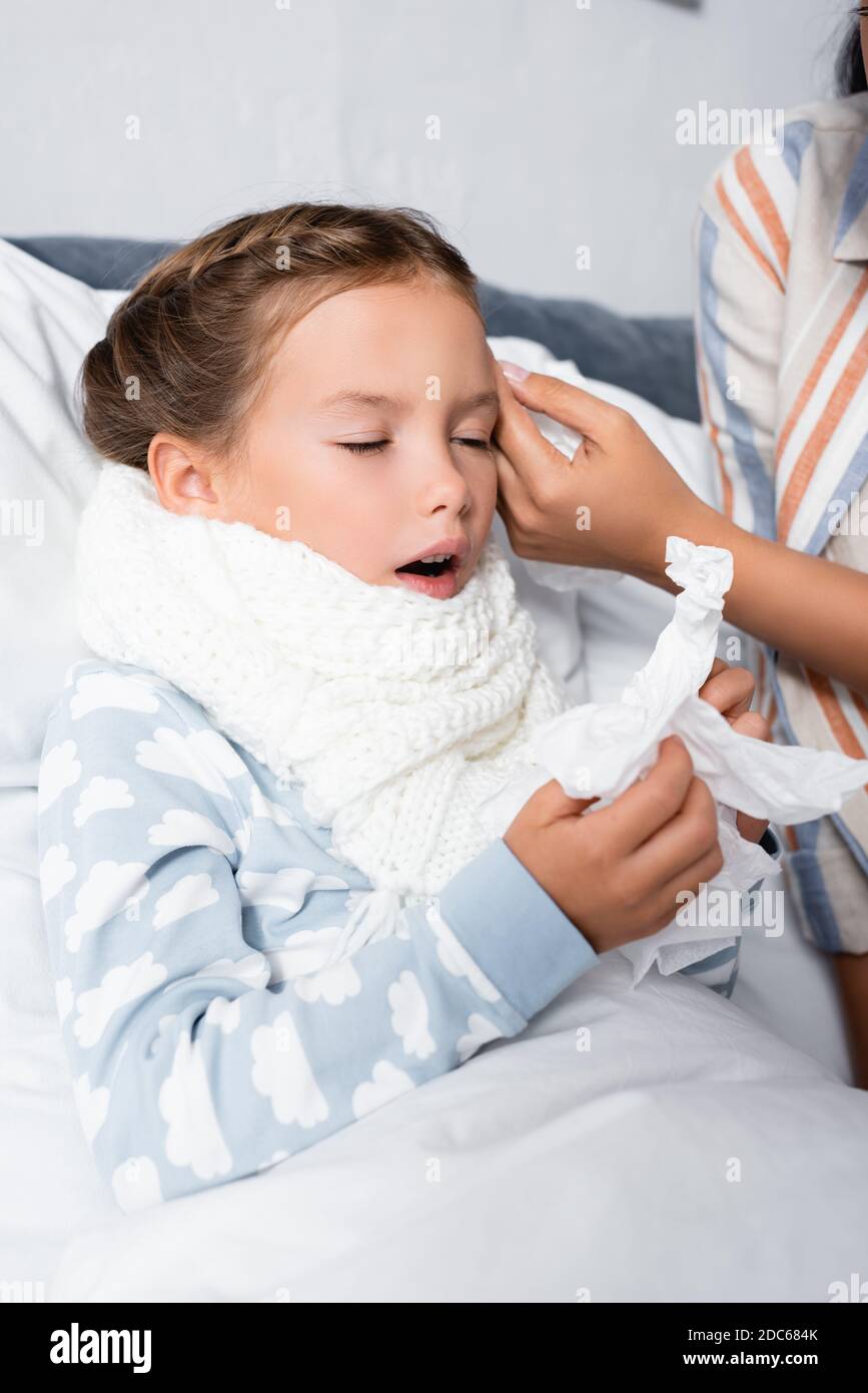 woman touching sick child lying in bed and holding paper napkins Stock ...