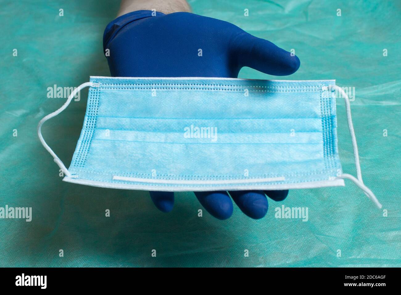 A hand protected with blue gloves shows a facial mask in the palm of ...
