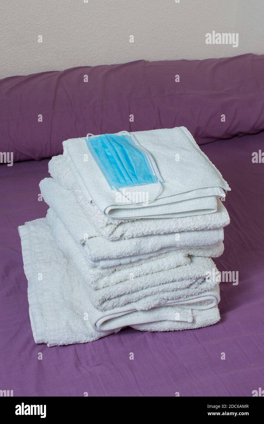 A surgical mask is on top of a stack of freshly washed white towels on ...