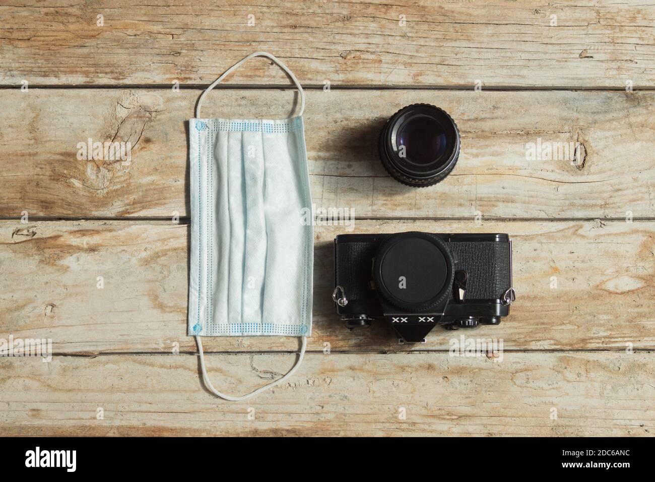 A surgical mask, a camera, and its lens are on top of an old wooden ...