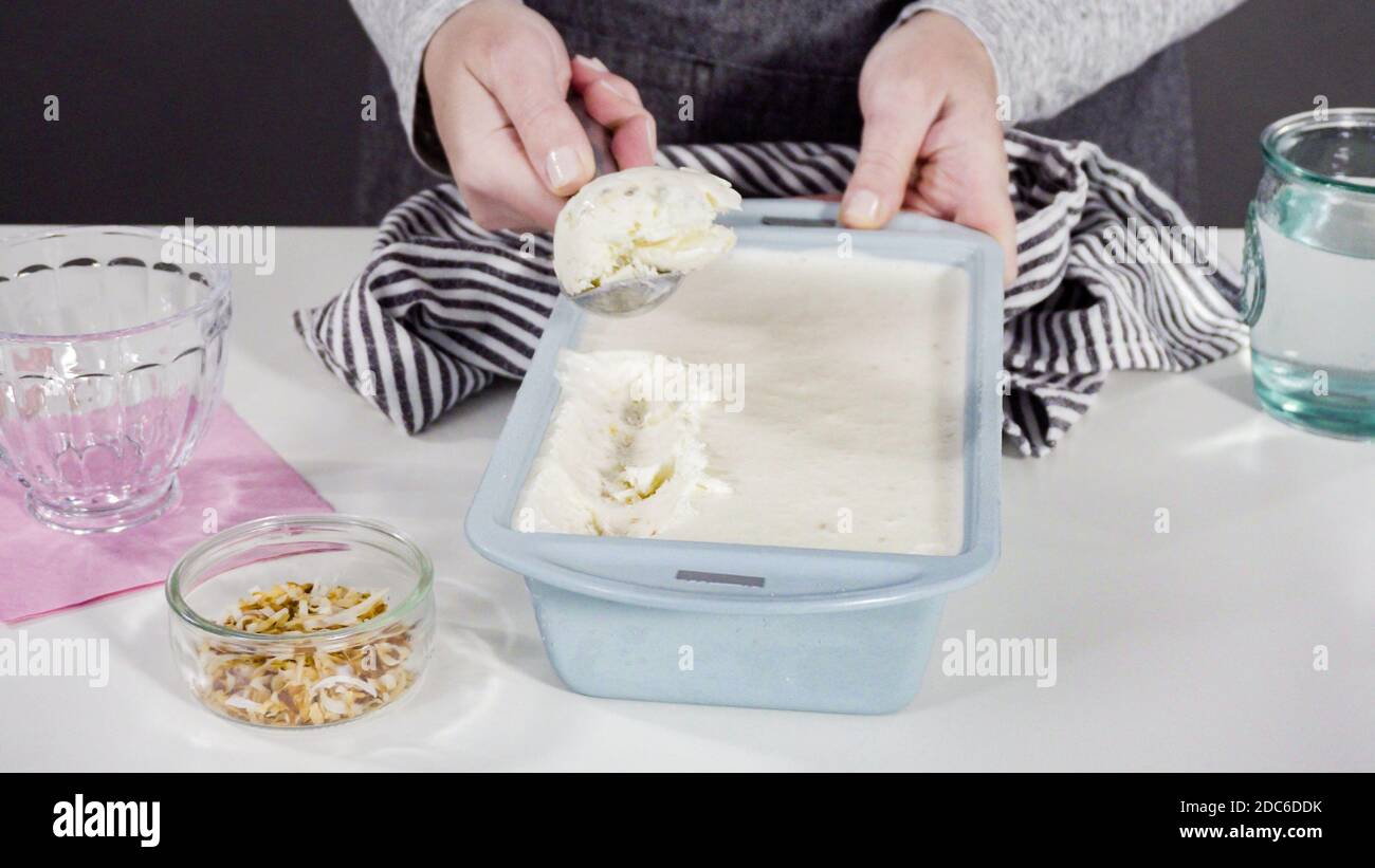 Scooping homemade coconut ice cream into a glass ice cream bowl Stock ...