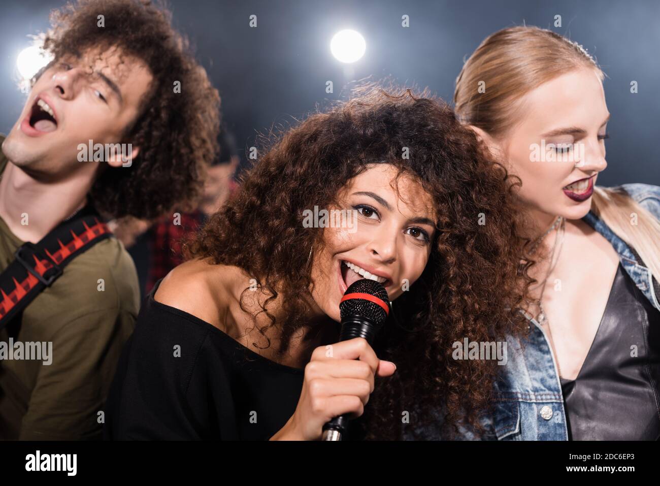 Happy rock band vocalist with microphone singing near musicians with ...