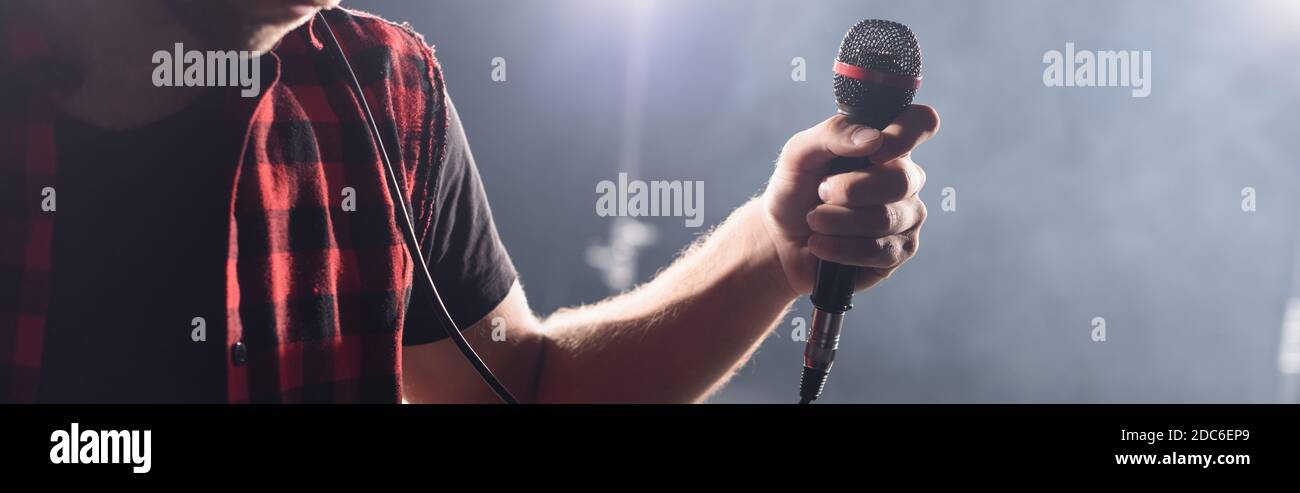 Cropped view of vocalist of rock band holding microphone on blurred ...