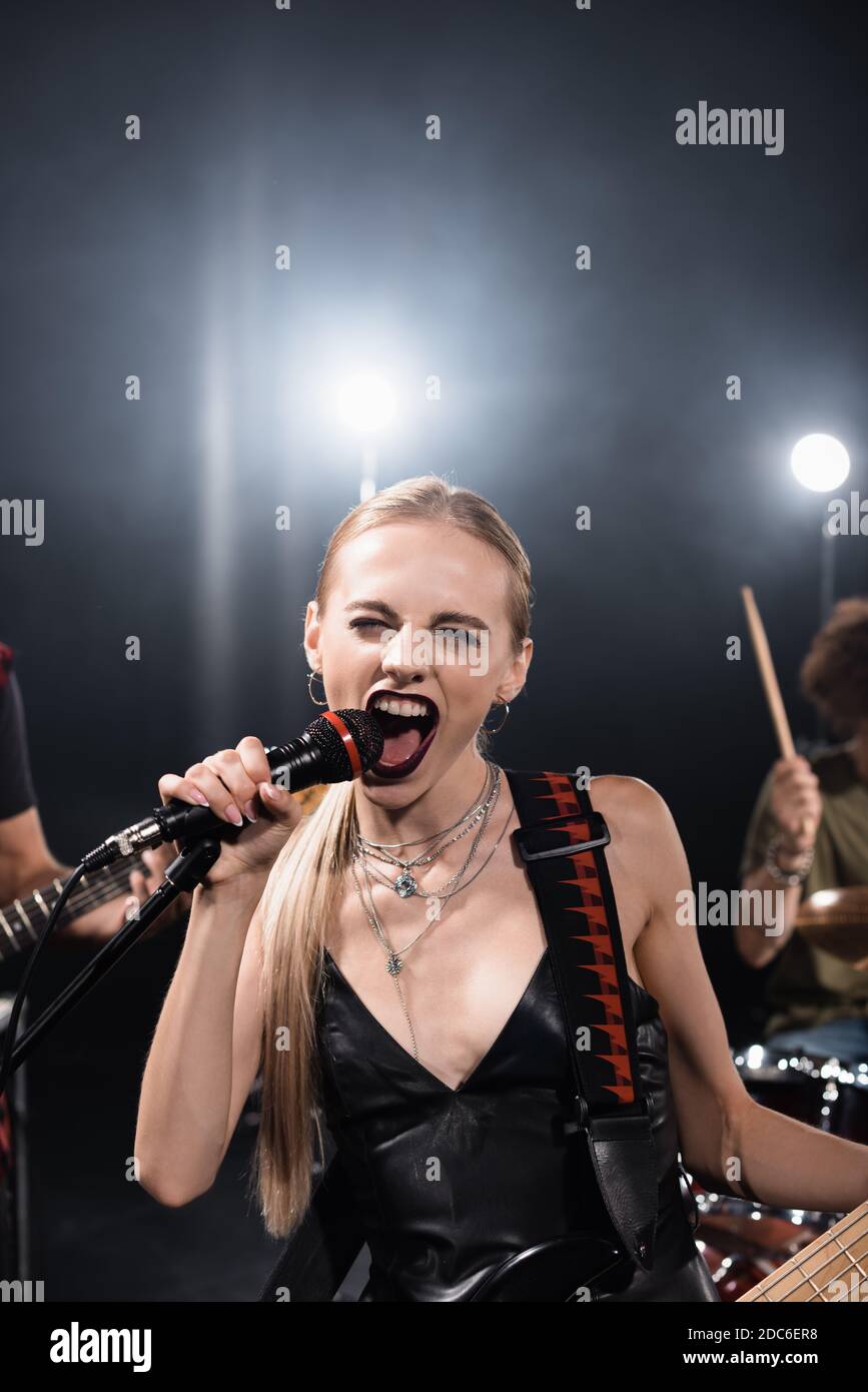 Blonde woman with bass guitar screaming in microphone with backlit and ...