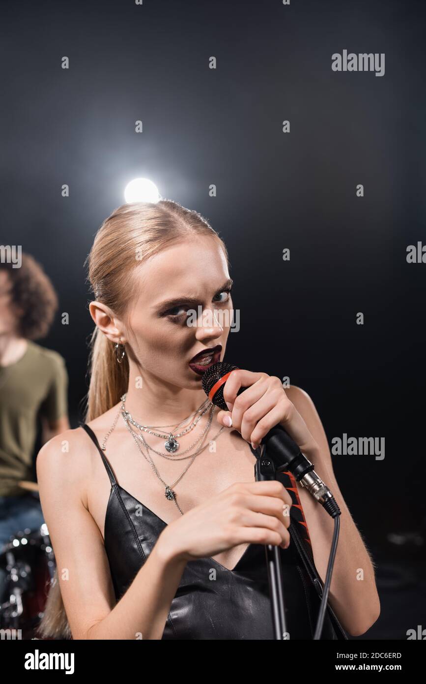 Angry blonde woman singing while touching microphone rack with backlit ...