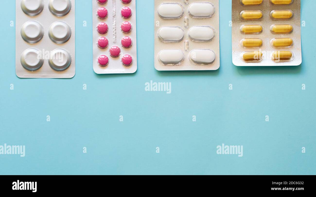 Layout of pink and white tablets and yellow capsules on a simple blue ...