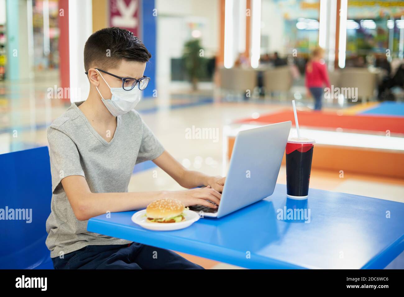 Teenager wearing protective mask uses laptop at fast food restaurant ...