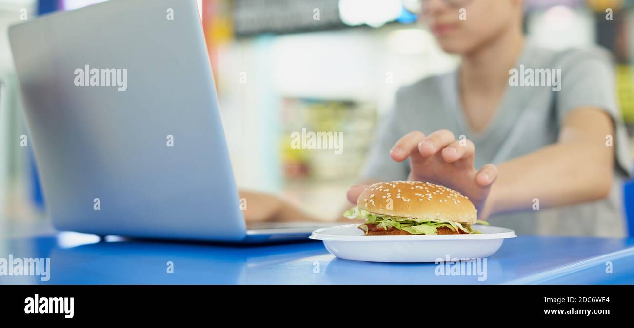 Teenager eating burger in fast food restaurant and using laptop Stock ...