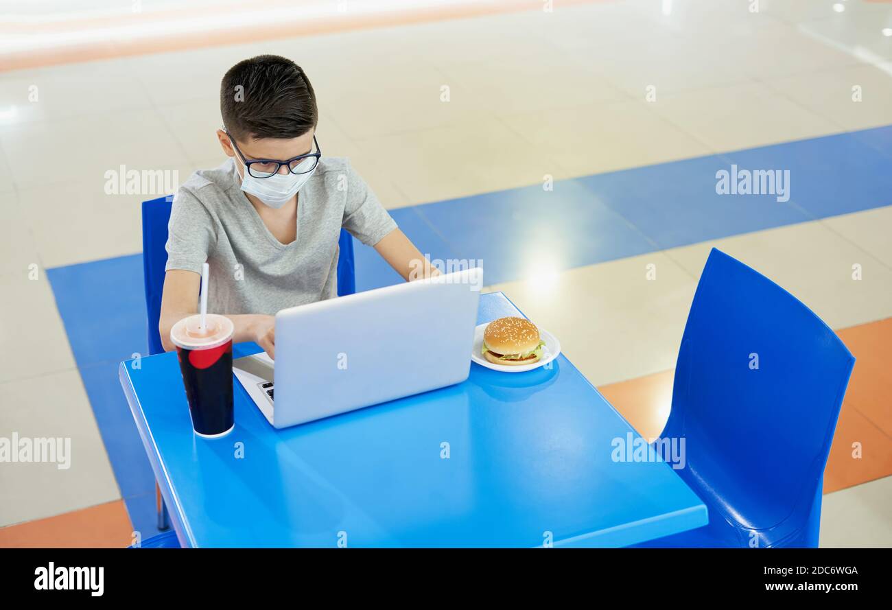 A teenager wearing a face mask uses a laptop at a fast food restaurant ...