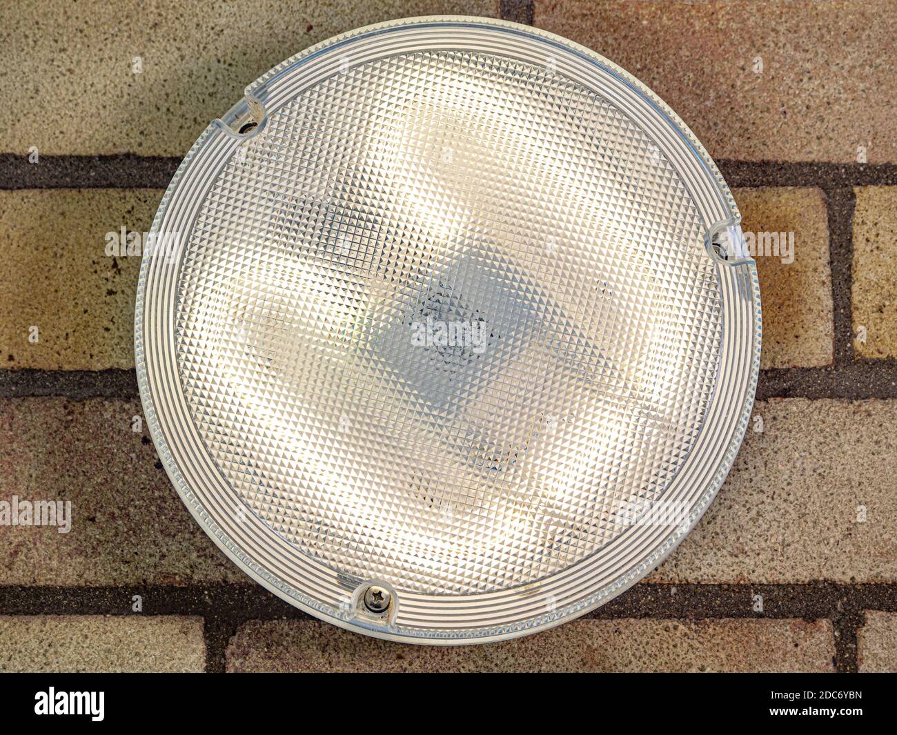 A circular, plastic covered, fluorescent energy saving light, mounted on an interior brick wall ...