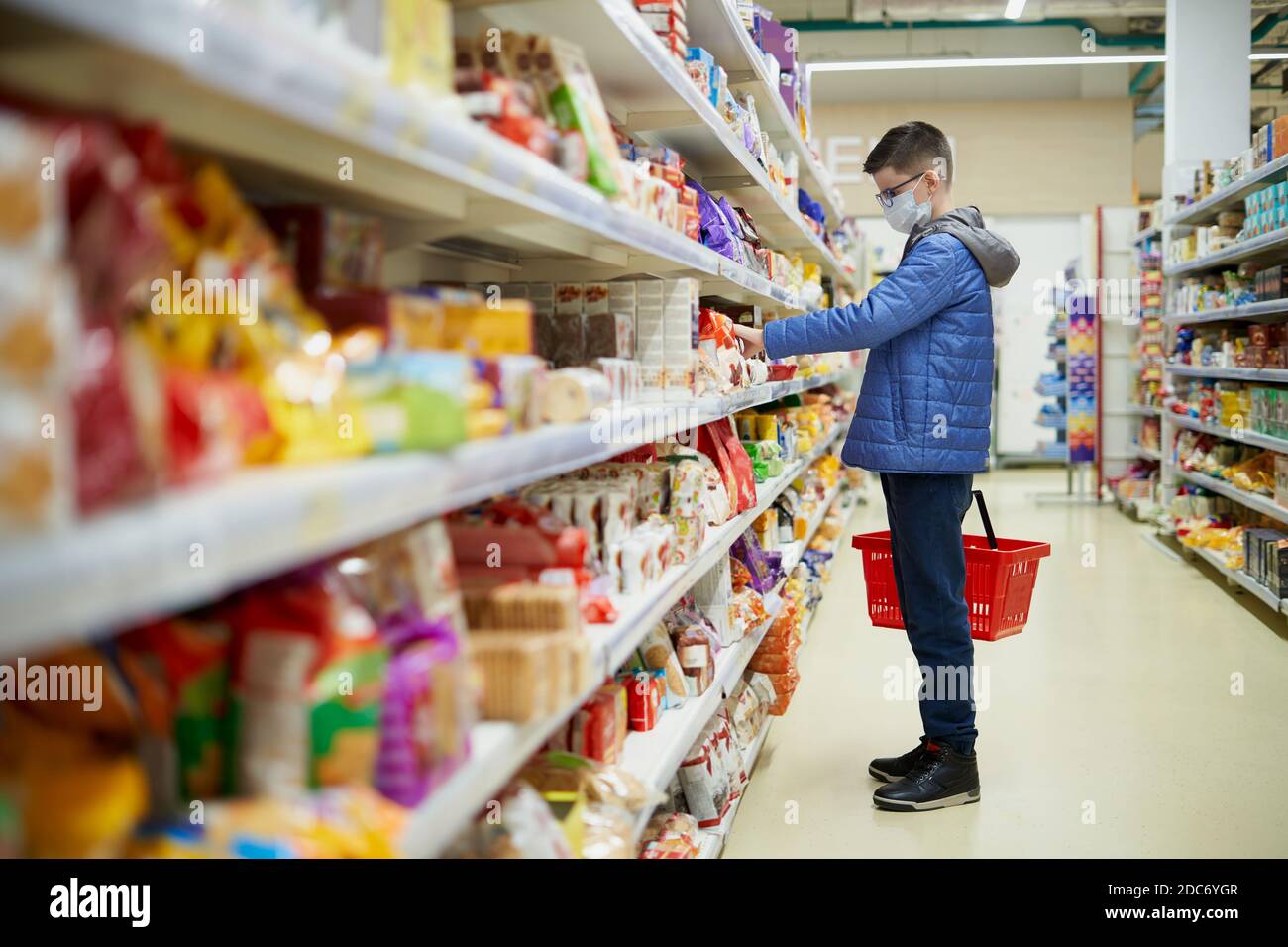 Boy teenager wearing a protective mask takes food from the shelf in a ...