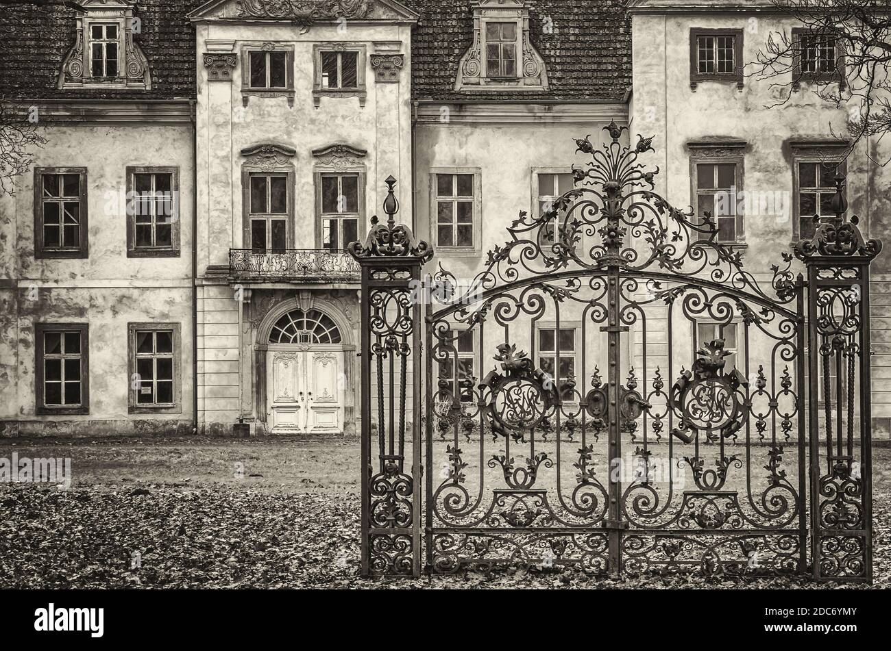 An old iron gate is placed in front of a dilapidated baroque manor ...