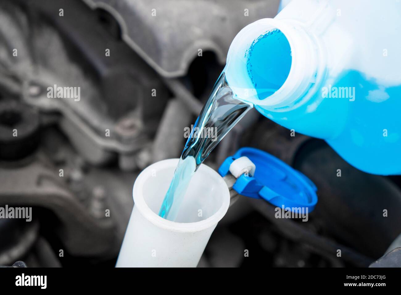 Pouring liquid from plastic canister into car washer fluid reservoir ...