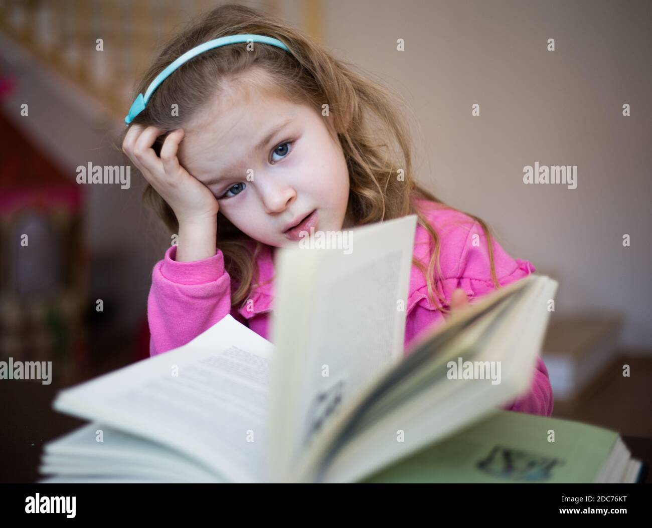 Little blonde girl reading and doing homework Stock Photo - Alamy
