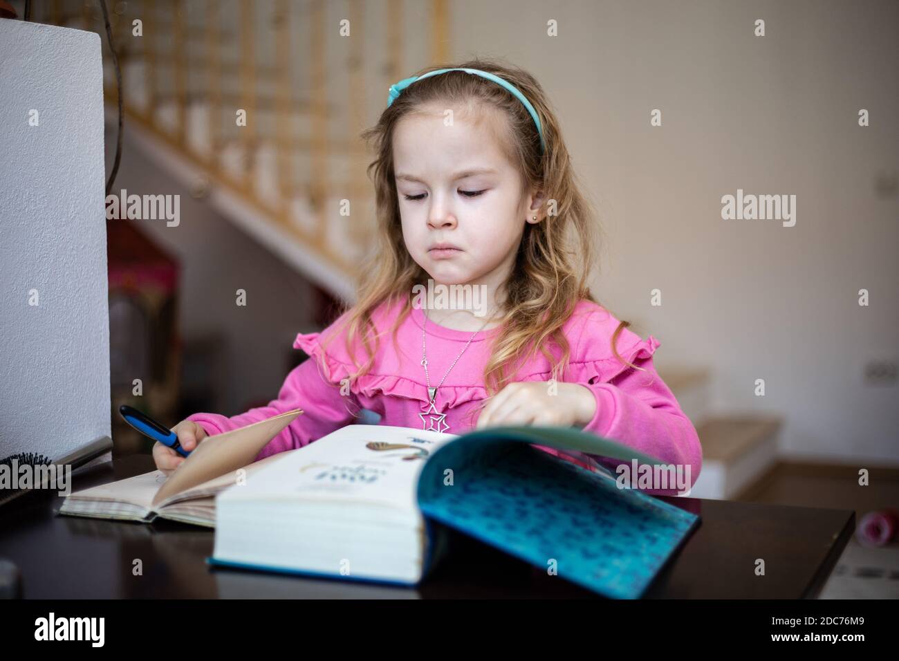 Little blonde girl reading and doing homework Stock Photo - Alamy